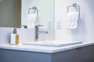 Casa de banho com lavatório branco, torneira cromada e um porta-toalhas com toalha branca.