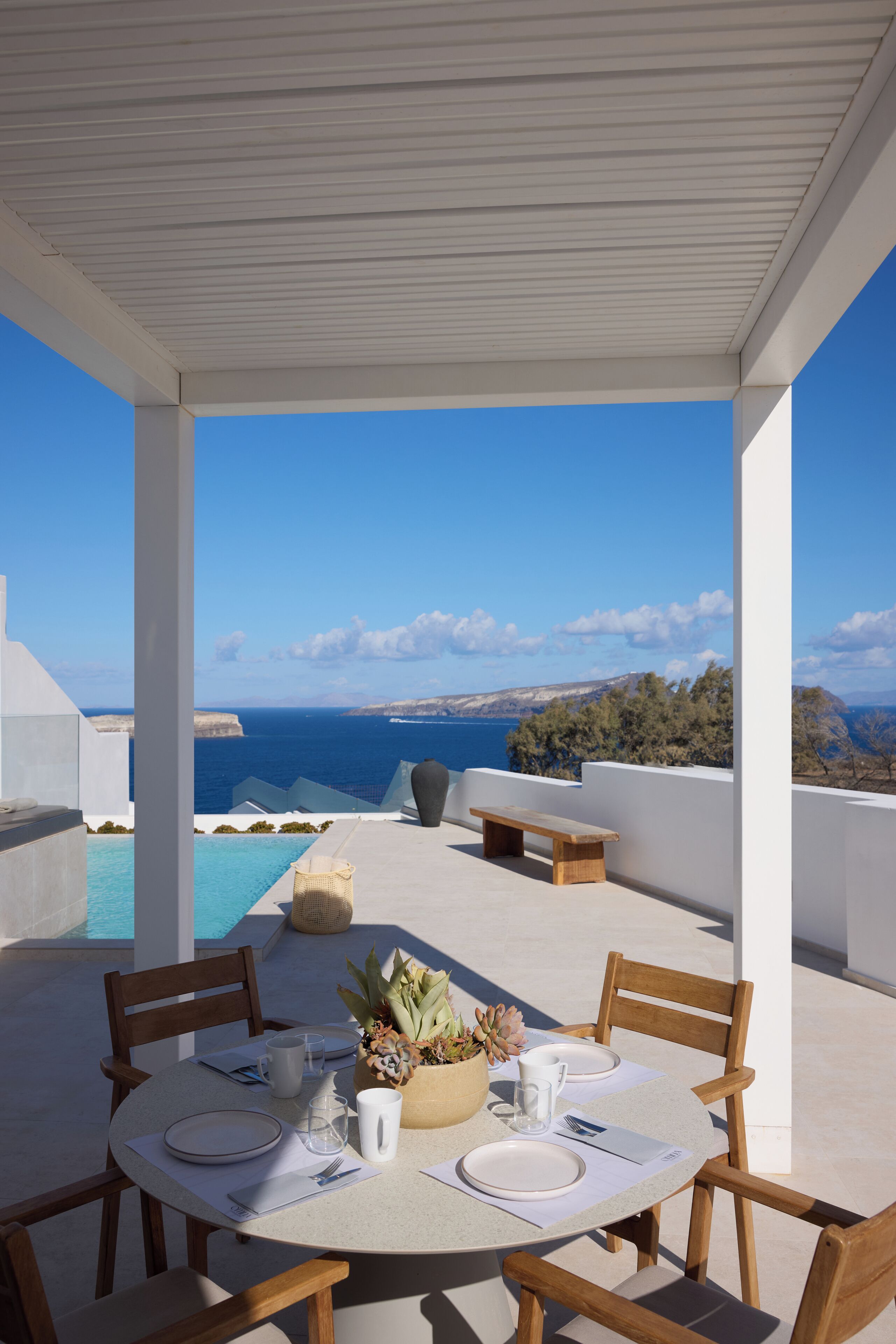 Área de refeições coberta ao ar livre, com uma mesa posta para dois, com vista para uma piscina e o mar.