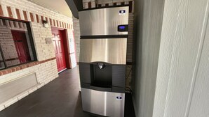 Um corredor com uma porta vermelha, um bebedouro e uma geladeira de aço inoxidável.