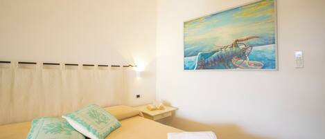 Quarto de hotel com cama, almofadas, um quadro, mesa de cabeceira e ar condicionado fixado na parede.