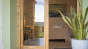 Quarto com cama, planta em vaso e vista para um jardim através de uma porta de vidro.