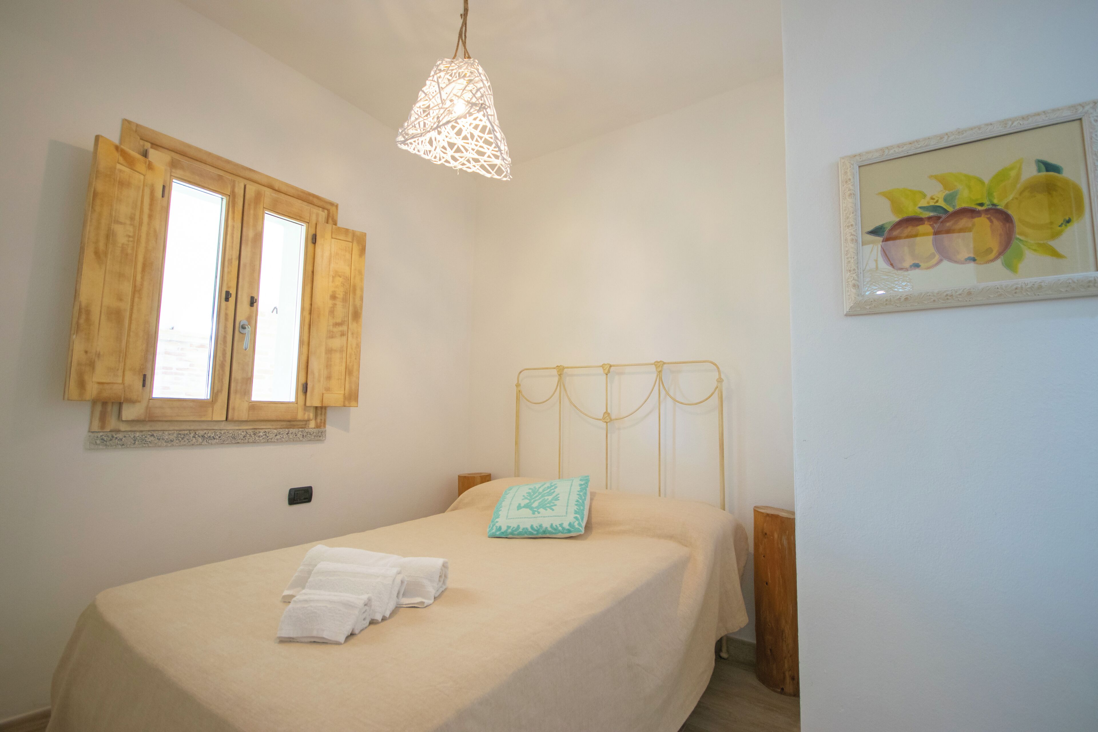 Um quarto com uma cama, luminária pendente, janela com persianas de madeira e um quadro na parede.