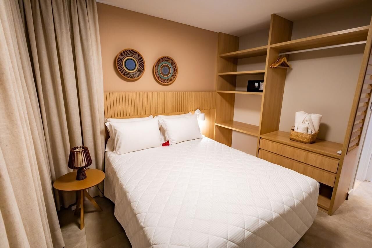 Quarto de hotel com uma cama, mesa de cabeceira com abajur, guarda-roupa e dois painéis decorativos na parede.