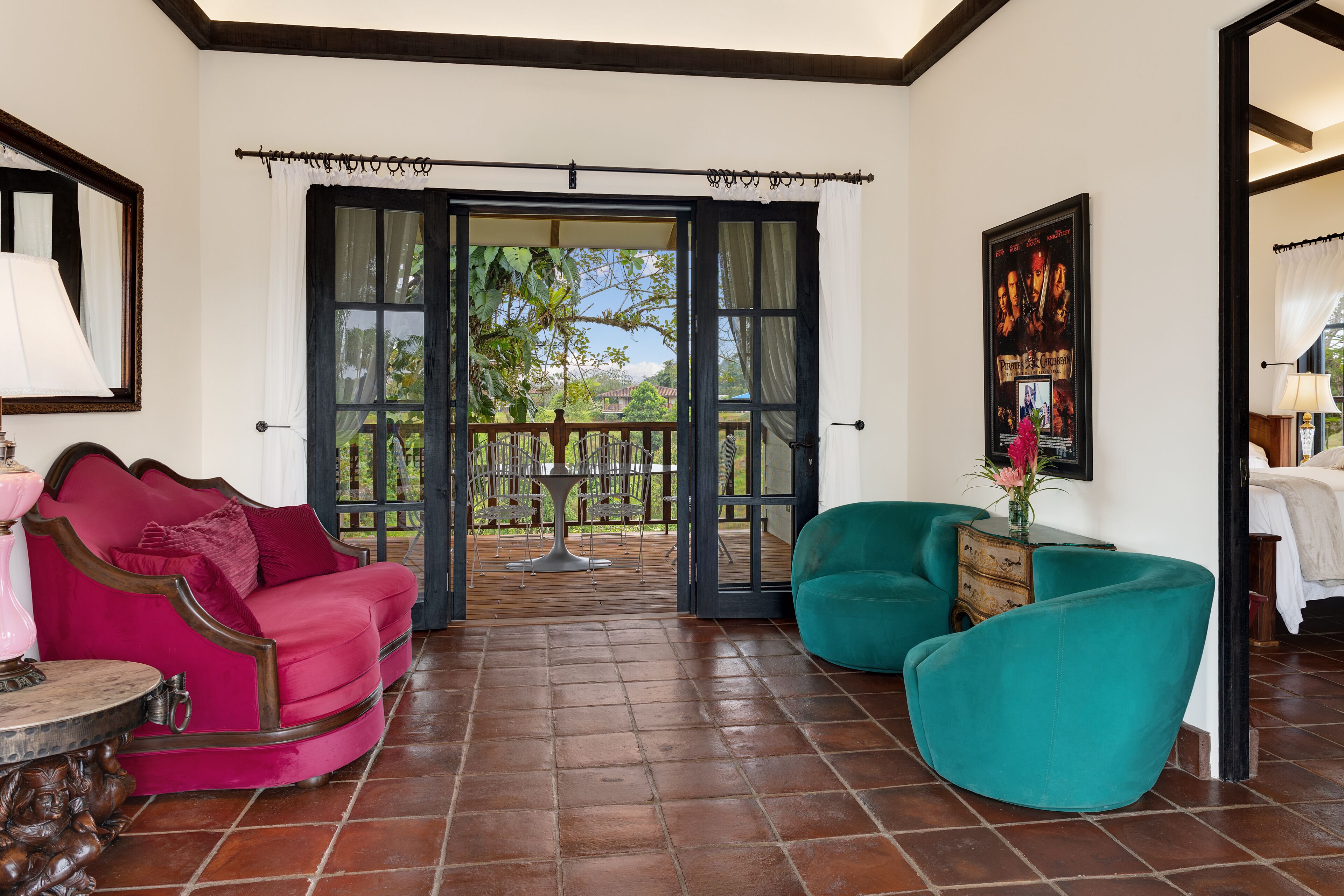 Quarto com sofá vermelho, poltronas verde-água, uma pequena mesa e varanda com vista.