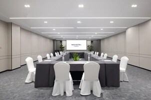 Uma sala de conferência com uma mesa comprida, cadeiras brancas e uma tela de projetor exibindo "NOVOTEL".