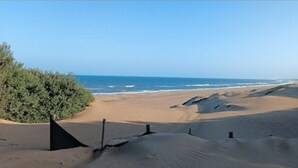 Uma praia arenosa com dunas suaves e uma vista clara do oceano.