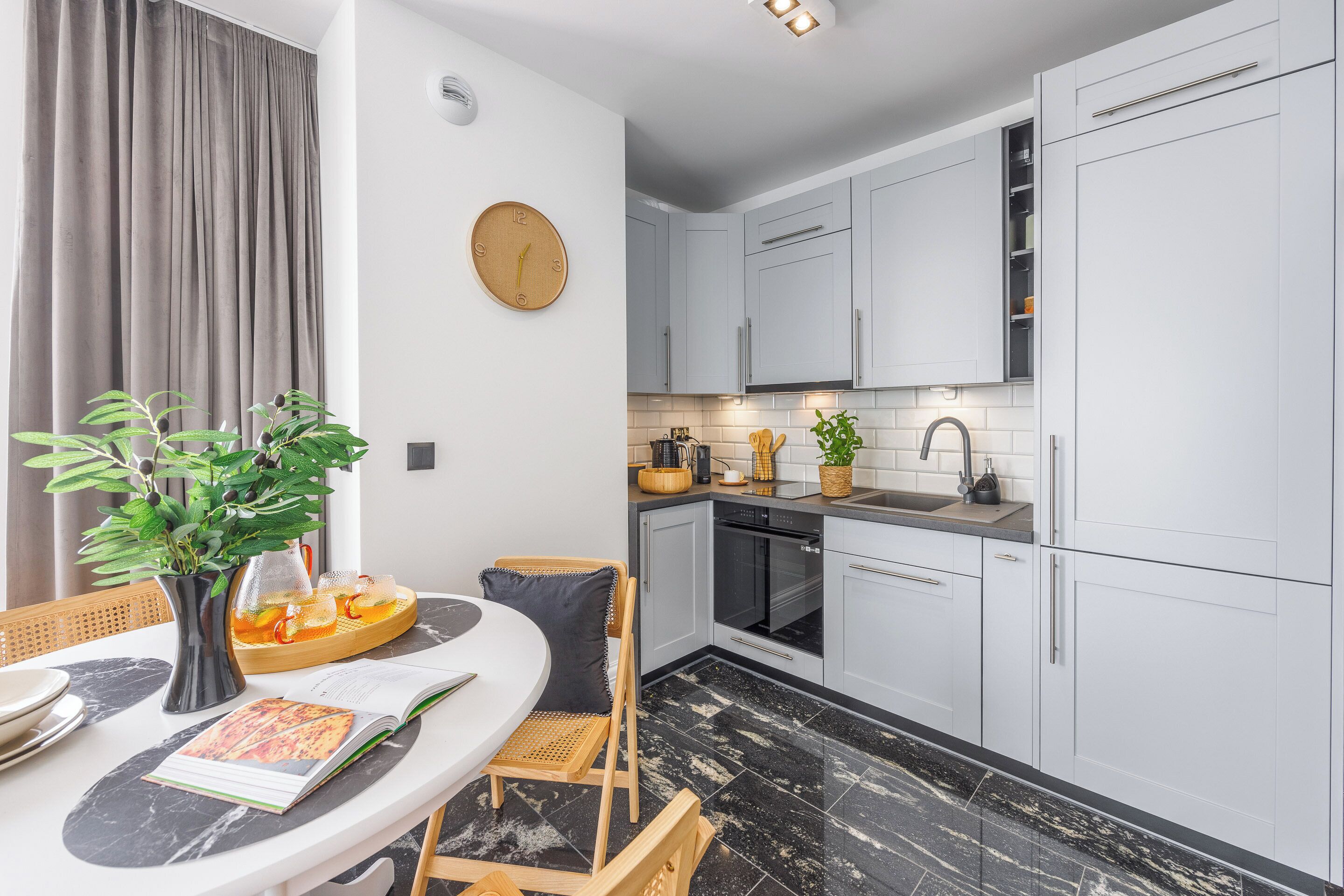 Cozinha moderna com armários brancos, piso de azulejos pretos e uma área de jantar com mesa e cadeiras redondas.