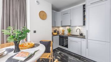 Cozinha moderna com armários brancos, piso de azulejos pretos e uma área de jantar com mesa e cadeiras redondas.