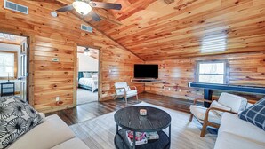 Interior de uma cabana de madeira com sala de estar, área de jantar e quarto.