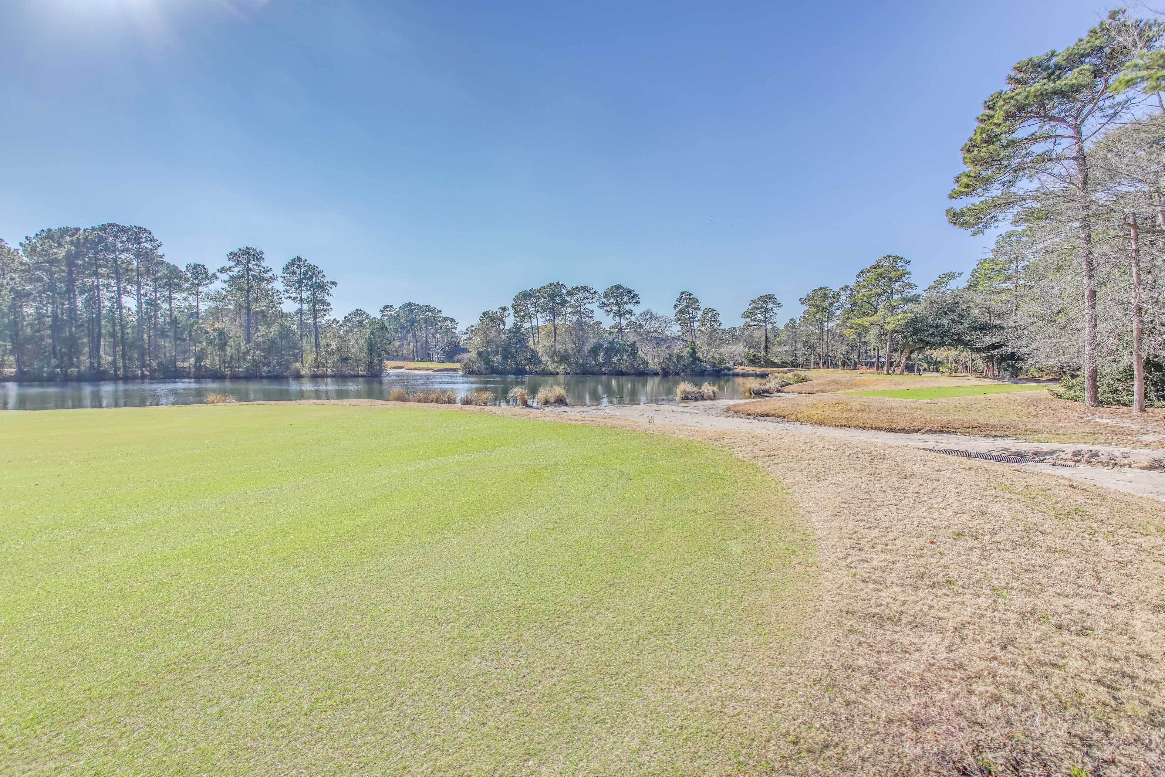 Um campo de golfe com um lago, árvores e céu claro.