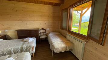 Quarto de cabana de madeira com duas camas, uma cômoda de madeira, uma cadeira e uma janela com vista para o verde.