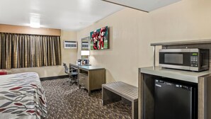 Quarto de hotel com cama, escrivaninha, micro-ondas, lava-louças, um banco, televisão e janela com cortinas.