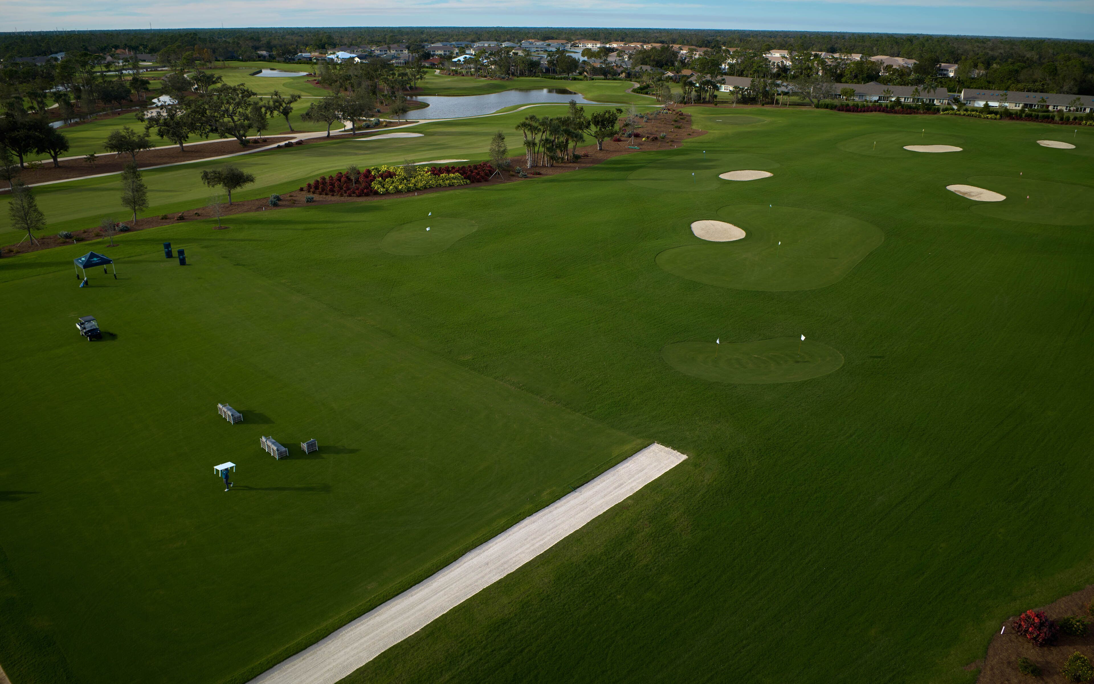 Um campo de golfe com bunkers de areia, lago e céu limpo.