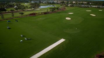 Um campo de golfe com bunkers de areia, lago e céu limpo.