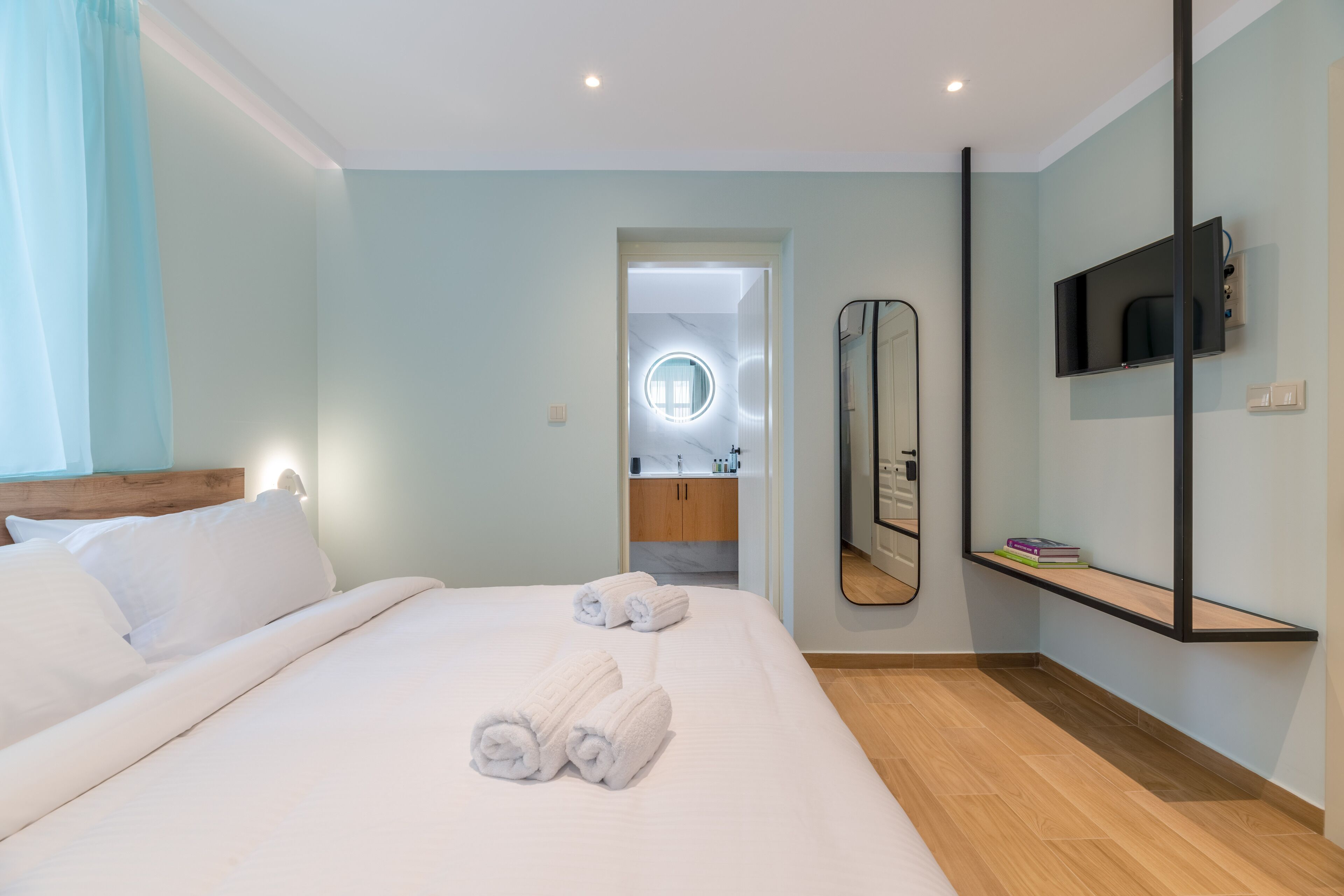 Quarto de hotel com uma cama grande, televisão montada na parede, espelho e vista para o banheiro.