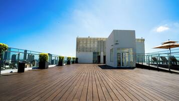 Terraço no telhado com deck de madeira, guarda-corpo de vidro e plantas em vasos.