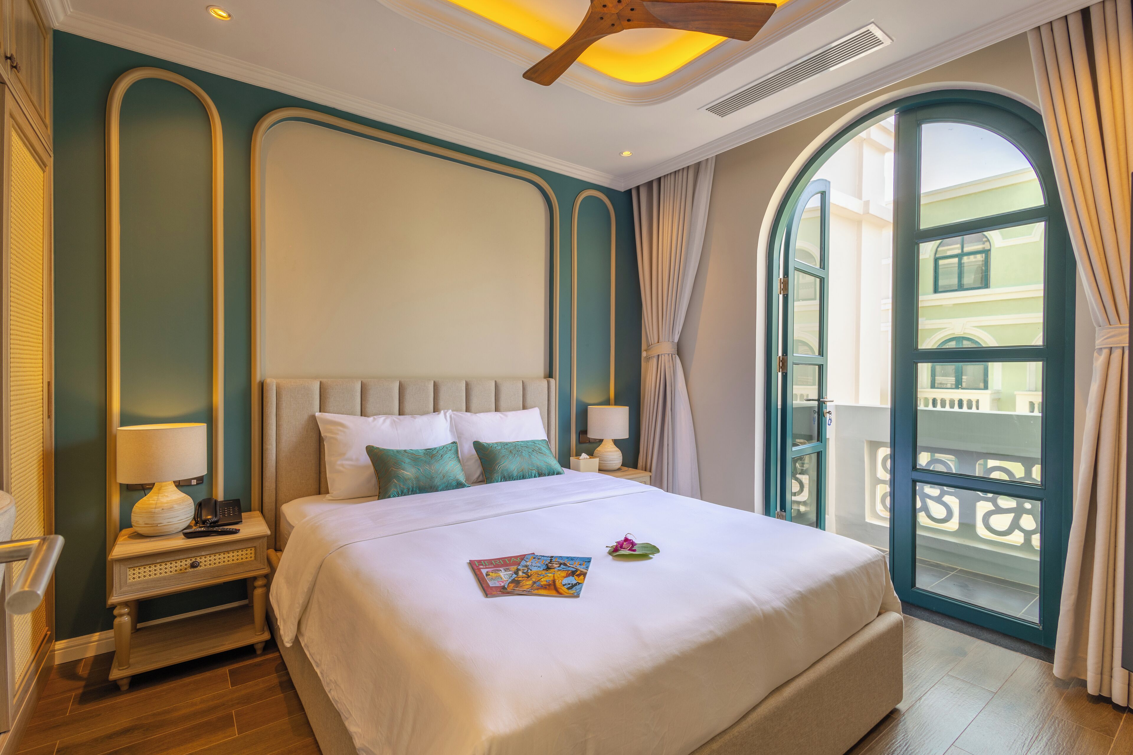 Quarto de hotel com uma cama grande, mesa de cabeceira com abajur, telefone e janela com cortinas.