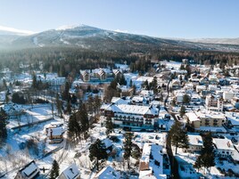 Uma cidade coberta de neve com uma mistura de edifícios residenciais e comerciais, incluindo um hotel de vários andares e uma construção grande com telhado inclinado.
