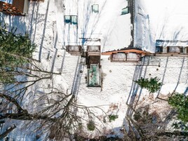 Vista aérea de um edifício com várias janelas e uma porta central, cercado por neve e árvores sem folhas.