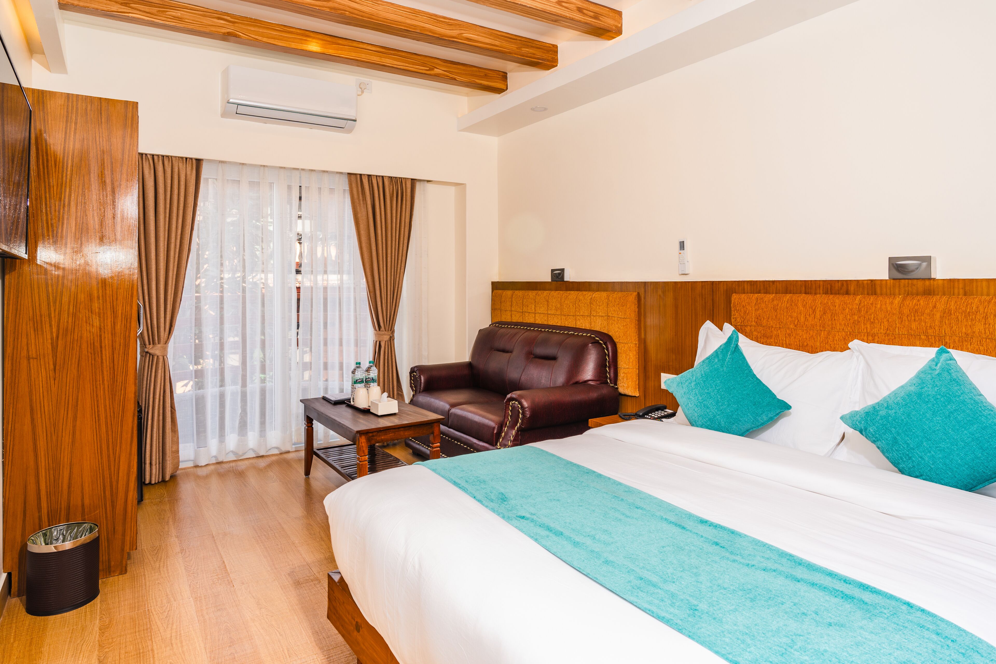 Quarto de hotel com uma cama grande, uma poltrona de couro, uma mesinha com garrafa e copos, e uma lixeira.