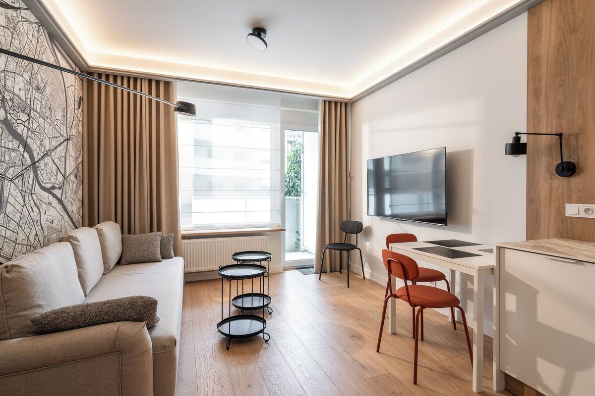 Uma sala de estar moderna com sofá, televisão, área de jantar e vista para o exterior.