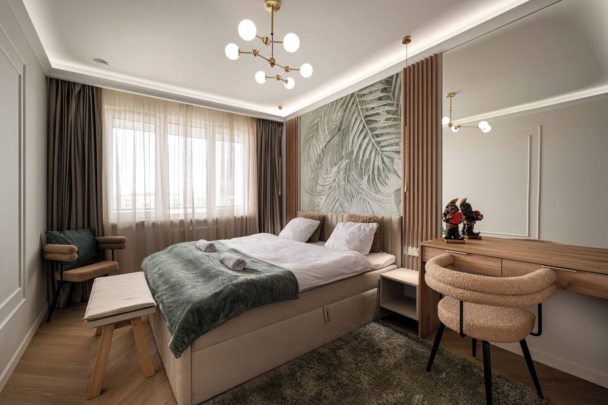Quarto moderno com cama, mesa de cabeceira, cadeira, escrivaninha e um espelho grande.