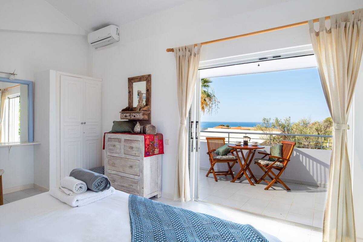Quarto com cama, cômoda, espelho e varanda com vista para o mar.