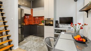 Cozinha compacta com eletrodomésticos modernos, área de refeições com mesa e televisão.