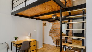 Quarto estilo loft com escrivaninha de madeira, uma cadeira, uma escada e parede de tijolos.