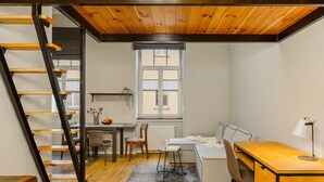 Quarto com teto de madeira, uma mesa com cadeira, radiador, janela e escada.