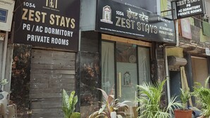 Um edifício com uma placa indicando ZEST STAYS, oferecendo dormitórios tipo PG/ar condicionado e quartos privativos.