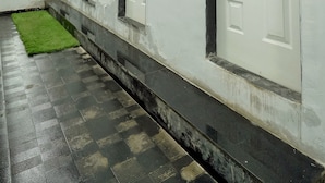 Corredor com paredes brancas, área com grama sintética verde e placa indicando que um banheiro está fechado.