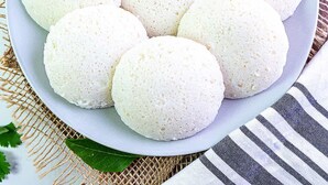 Prato com pedaços brancos e redondos, possivelmente idlis, acompanhados de uma tigela de curry e uma tigela de molho branco com especiarias.