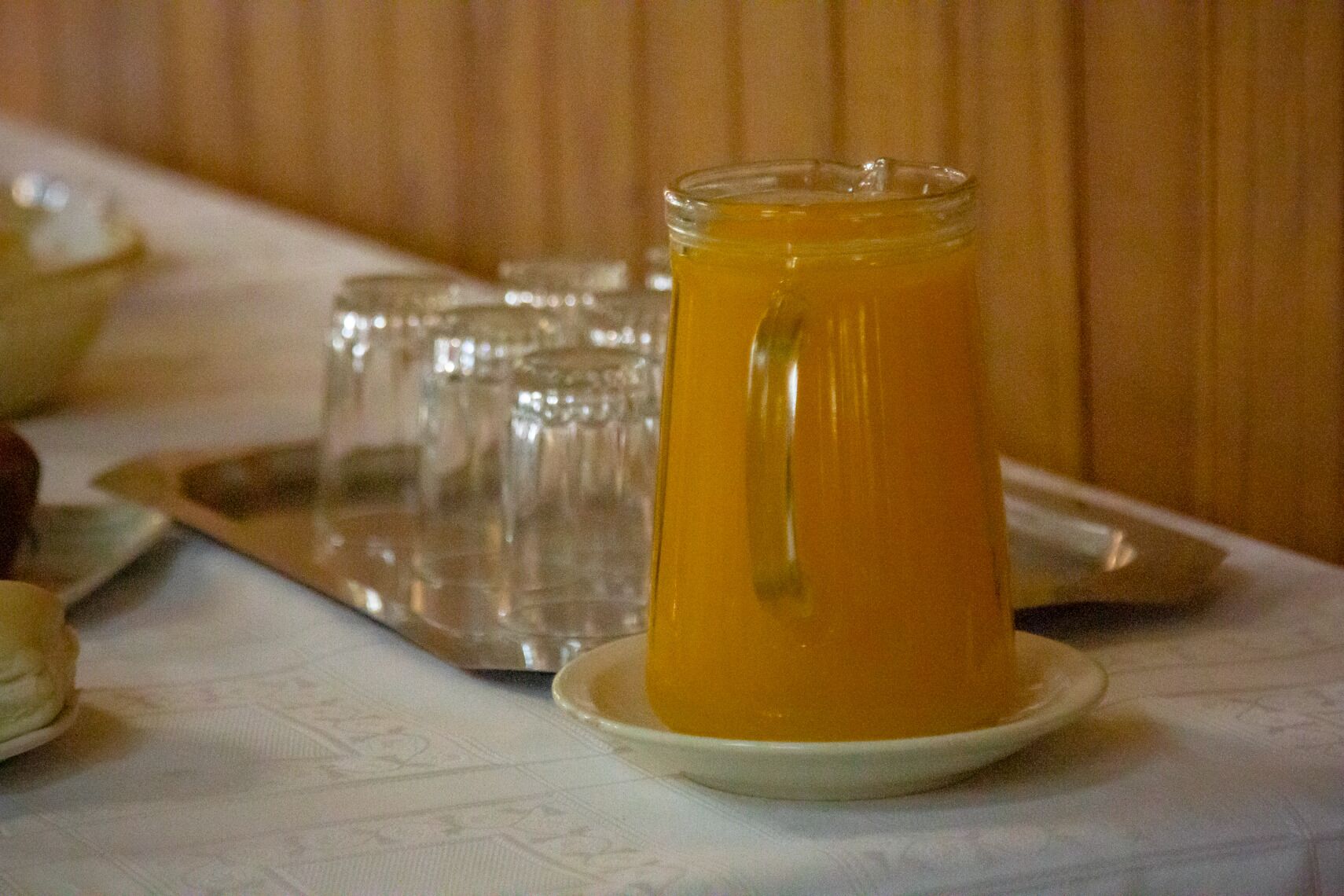 Um copo de suco de laranja sobre um prato branco, com uma bandeja de copos ao fundo.