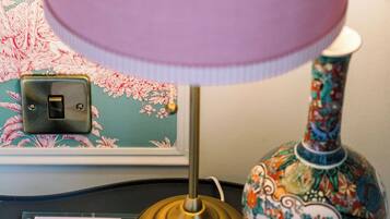 Uma luminária com cúpula rosa, um vaso decorativo, uma caneta e um bloco de notas sobre uma mesa.