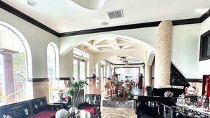 Um hall espaçoso com um piano de cauda, uma área de estar com um sofá vermelho e um globo decorativo como peça central.