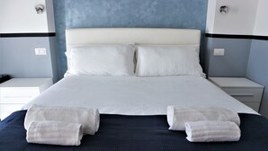 Cama bem arrumada com roupa de cama branca e duas toalhas colocadas ao pé da cama.