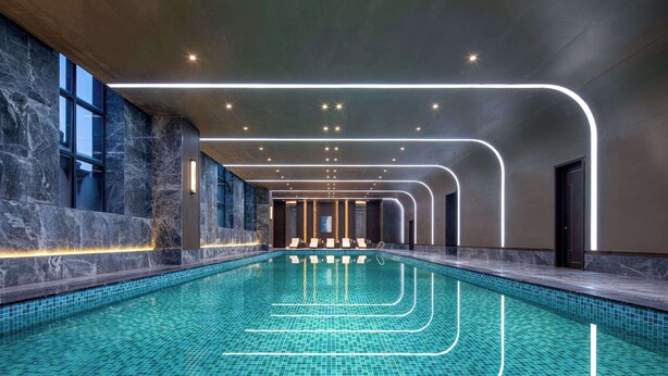 Piscina interior moderna com água cristalina, rodeada por paredes de mármore e design contemporâneo elegante.