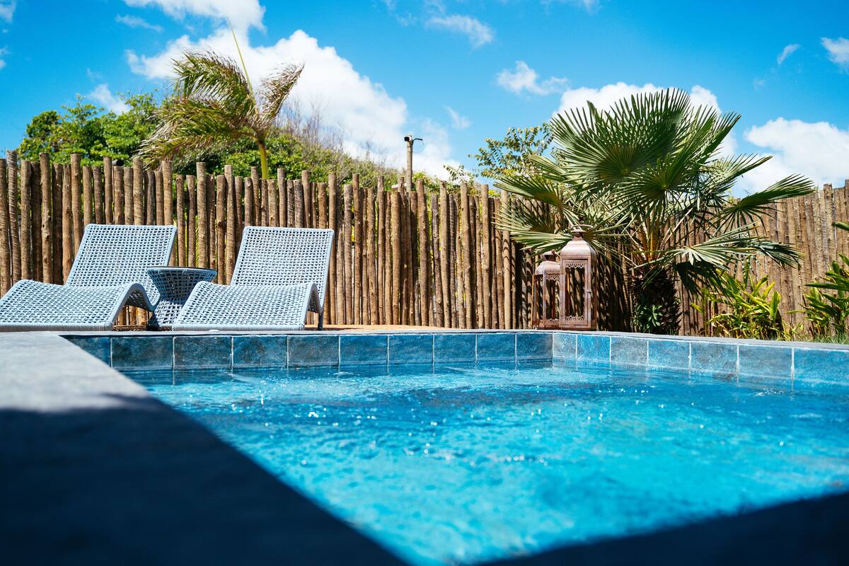 Piscina com duas espreguiçadeiras e um cercado de bambu ao fundo.