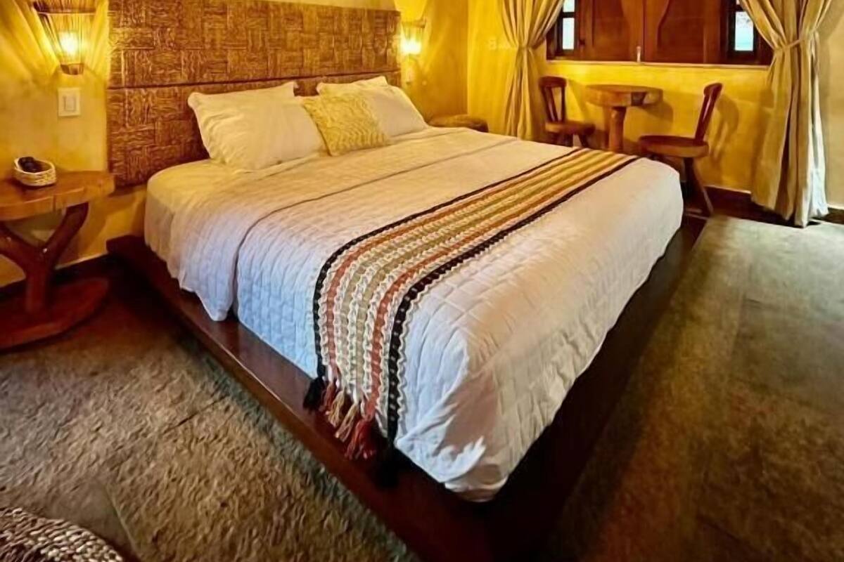Quarto com uma cama grande, luminária de teto trançada, cabeceira de madeira e uma pequena mesa com cadeiras.
