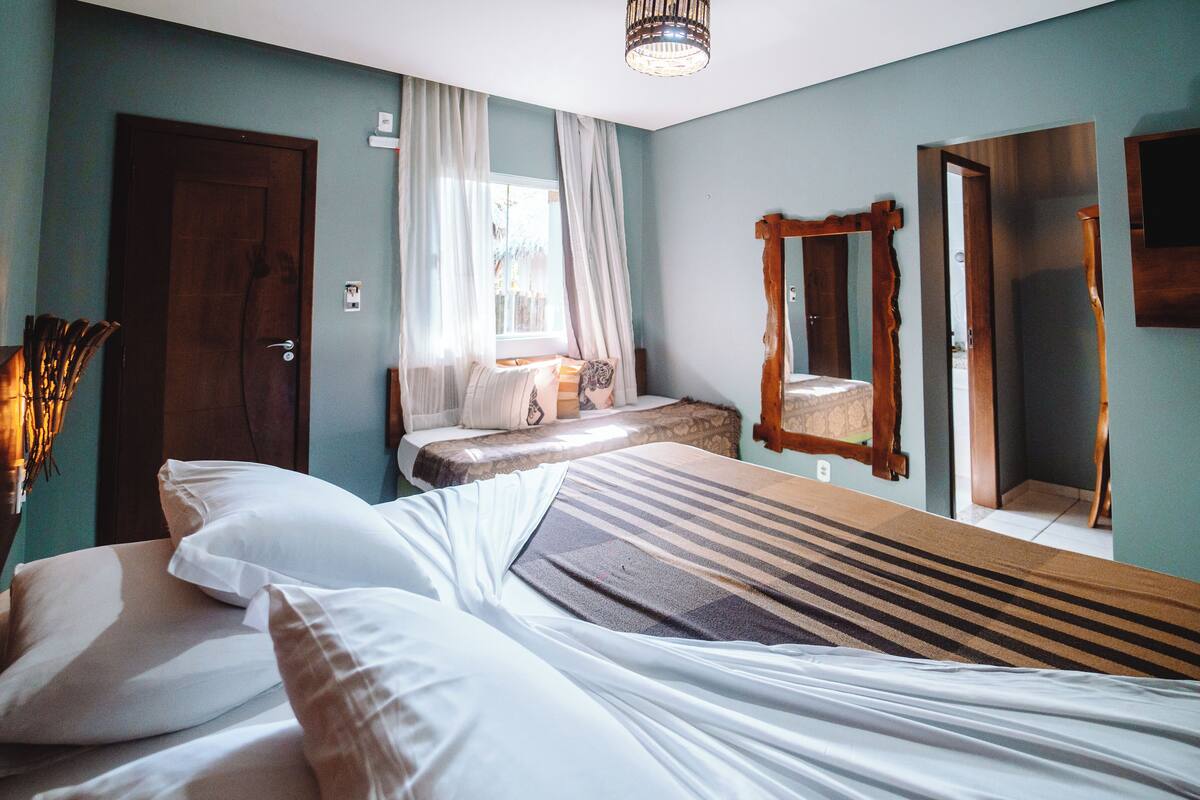 Quarto com duas camas, porta de madeira, espelho e janela com cortinas.