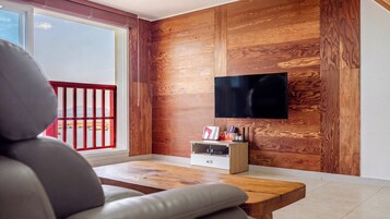 Sala de estar moderna com painel de parede de madeira, televisão de tela plana fixada acima de um armário de madeira, e vista para uma varanda vermelha.