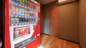 Máquina automática com bebidas e petiscos, uma porta de madeira e um aparelho de ar condicionado na parede.