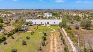 Um grande edifício branco com um pátio central, rodeado por vegetação e um céu claro.