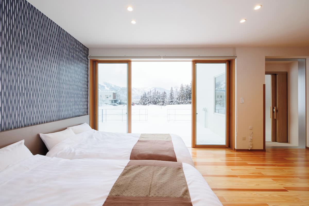 Quarto de hotel moderno com uma cama grande, vista para montanhas nevadas e uma porta de vidro deslizante que dá para uma varanda.