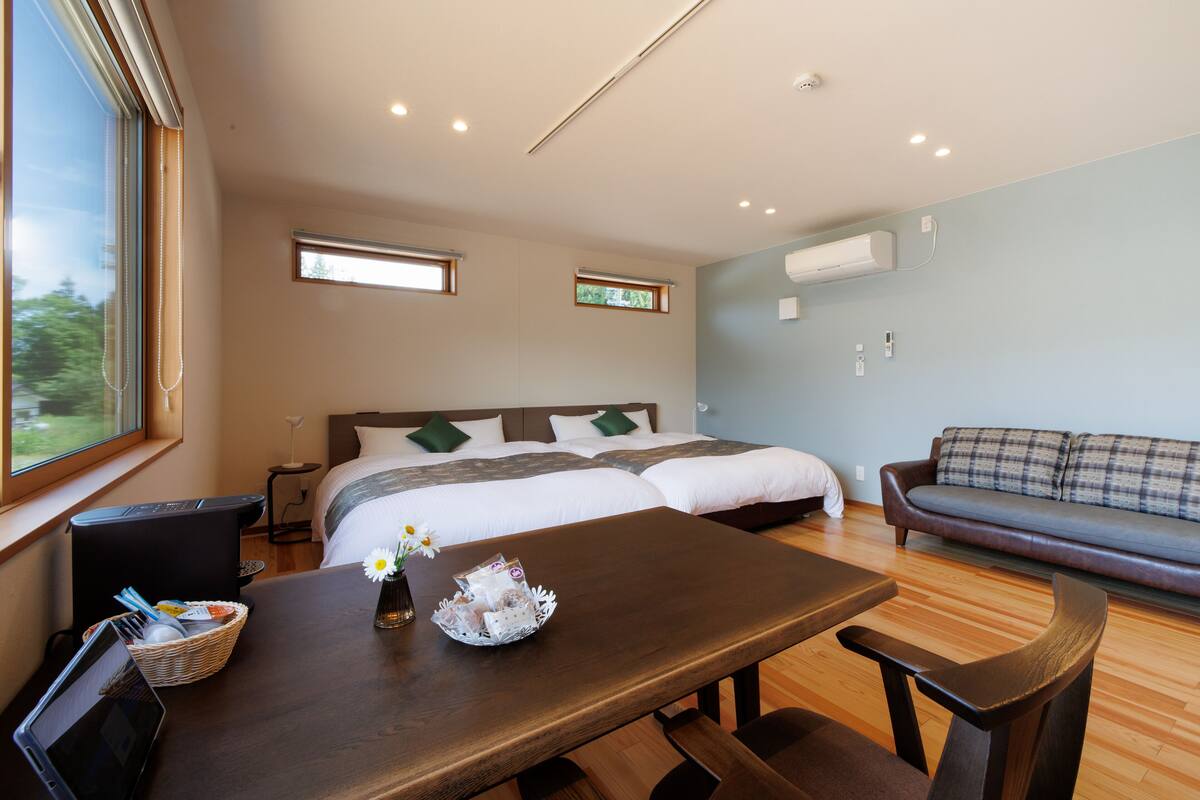 Quarto de hotel com uma cama grande, um sofá, uma mesa de jantar e vista para o exterior.