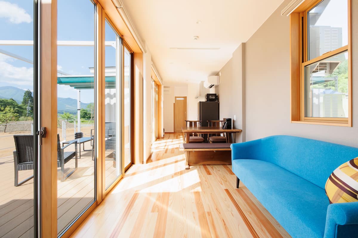 Interior moderno com sofá azul, piso de madeira e amplas portas de vidro deslizantes que dão para um deck externo.
