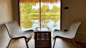 Quarto com duas cadeiras voltadas para uma janela grande com vista para um lago e árvores.