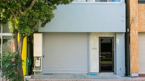 Vitrine fechada com toldo metálico, porta visível com a inscrição "RO SPACE" e uma árvore com folhas verdes à esquerda.