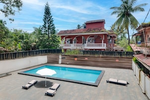 Piscina com espreguiçadeiras e um edifício vermelho com varanda ao fundo.